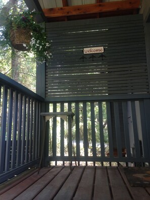 Um deck de madeira com uma placa de 'Welcome', um vaso suspenso e um guarda-corpo de metal.