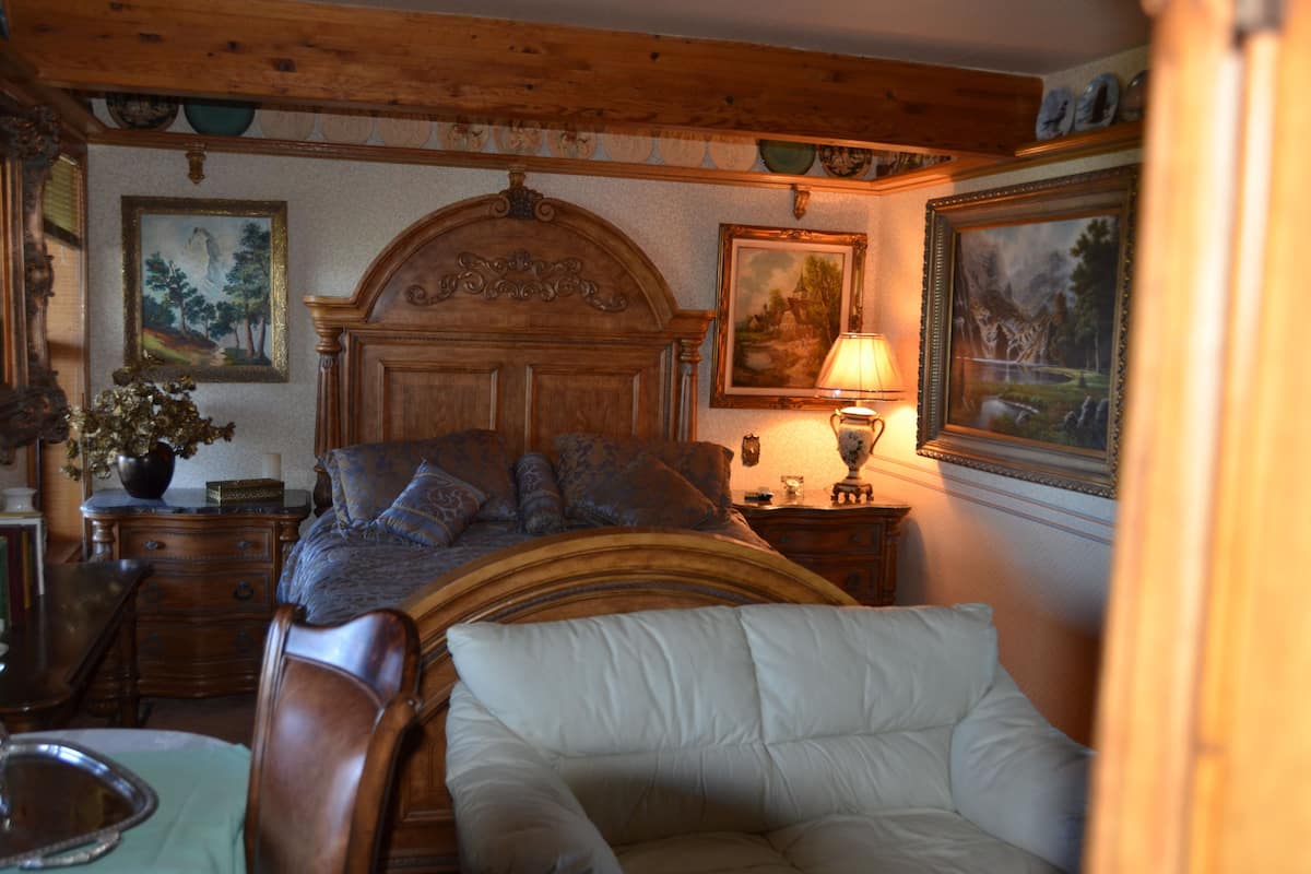Um quarto com uma cama de madeira, uma mesinha de cabeceira com abajur, e duas pinturas emolduradas de paisagens na parede.