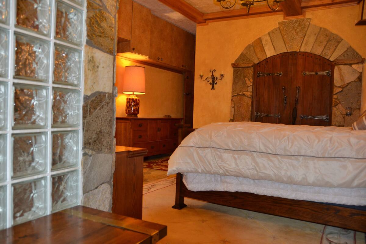 Quarto com parede de pedra, cama de madeira, lareira de pedra e guarda-roupa de madeira.