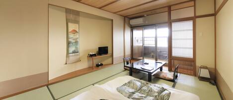 Um quarto japonês tradicional com tatames, futon, porta deslizante, televisão e um biombos shoji.