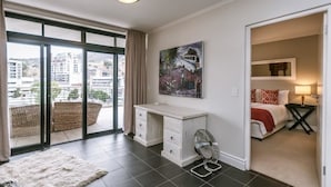 Quarto moderno com uma grande porta de vidro deslizante que dá para uma varanda, cômoda branca, uma pintura e uma área de cama aconchegante.