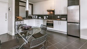 Uma cozinha moderna com armários brancos, eletrodomésticos de aço inoxidável e uma mesa de jantar de vidro.