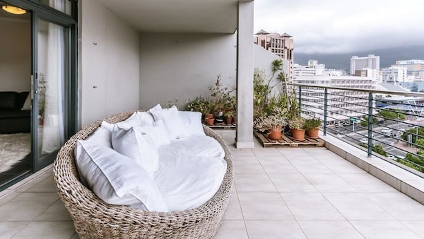 Uma varanda com sofá de vime, plantas em vasos e vista para a cidade.