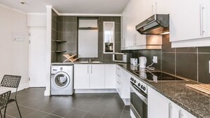 Cozinha compacta com máquina de lavar, micro-ondas, fogão e um espaço de refeições com uma cadeira.
