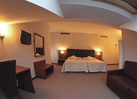 Quarto de hotel com cama de casal, escrivaninha, cadeira, televisão e um espelho grande.