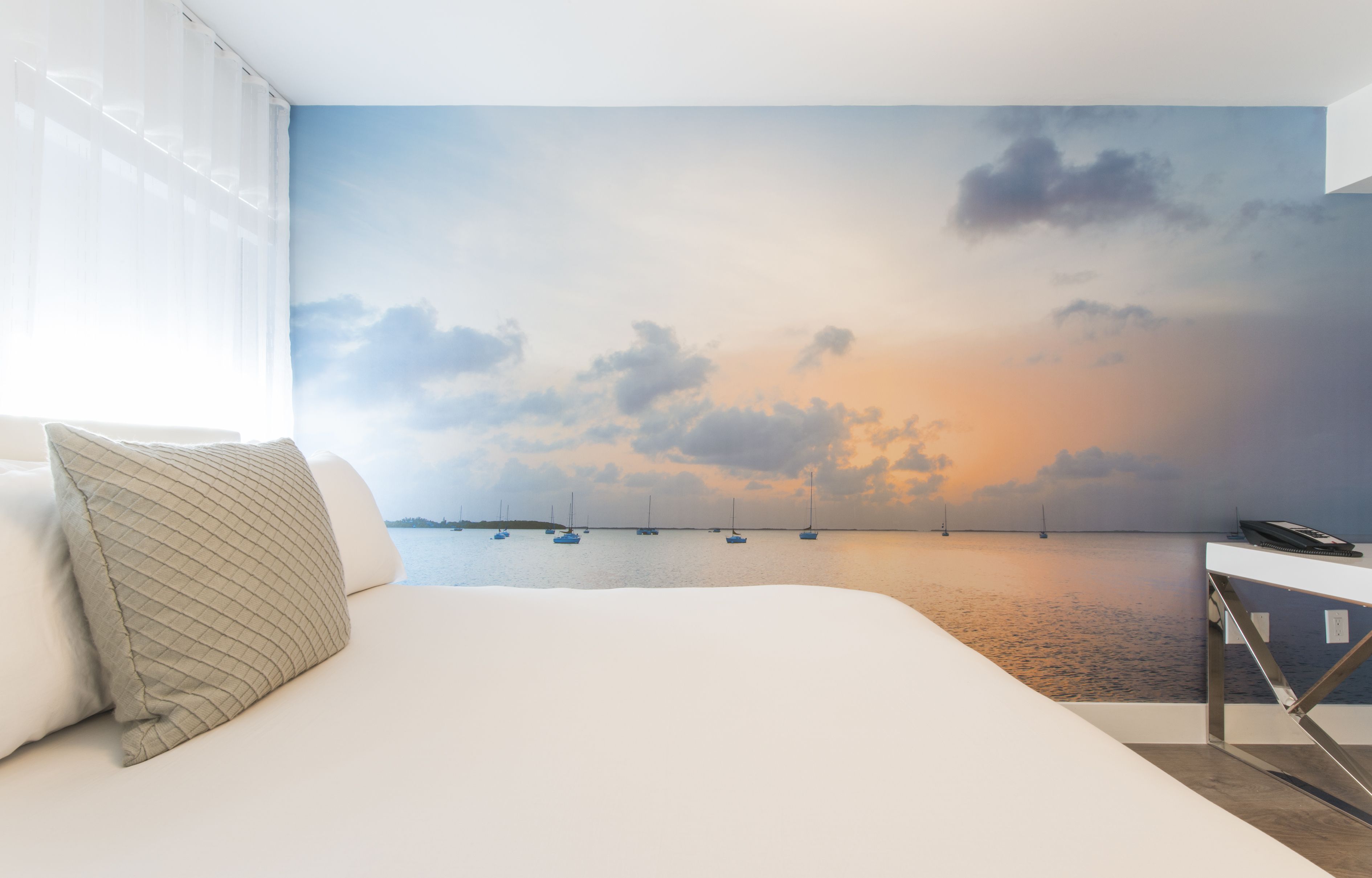 Quarto de hotel com cama, escrivaninha e vista para o mar, incluindo barcos.