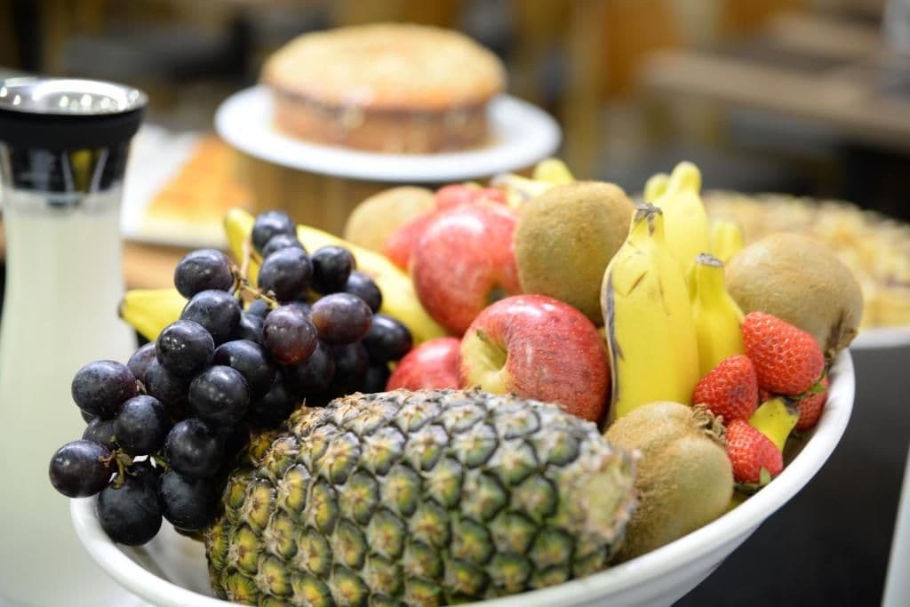 Uma tigela com frutas variadas, incluindo uvas, maçãs, bananas, kiwis e uma abacaxi.