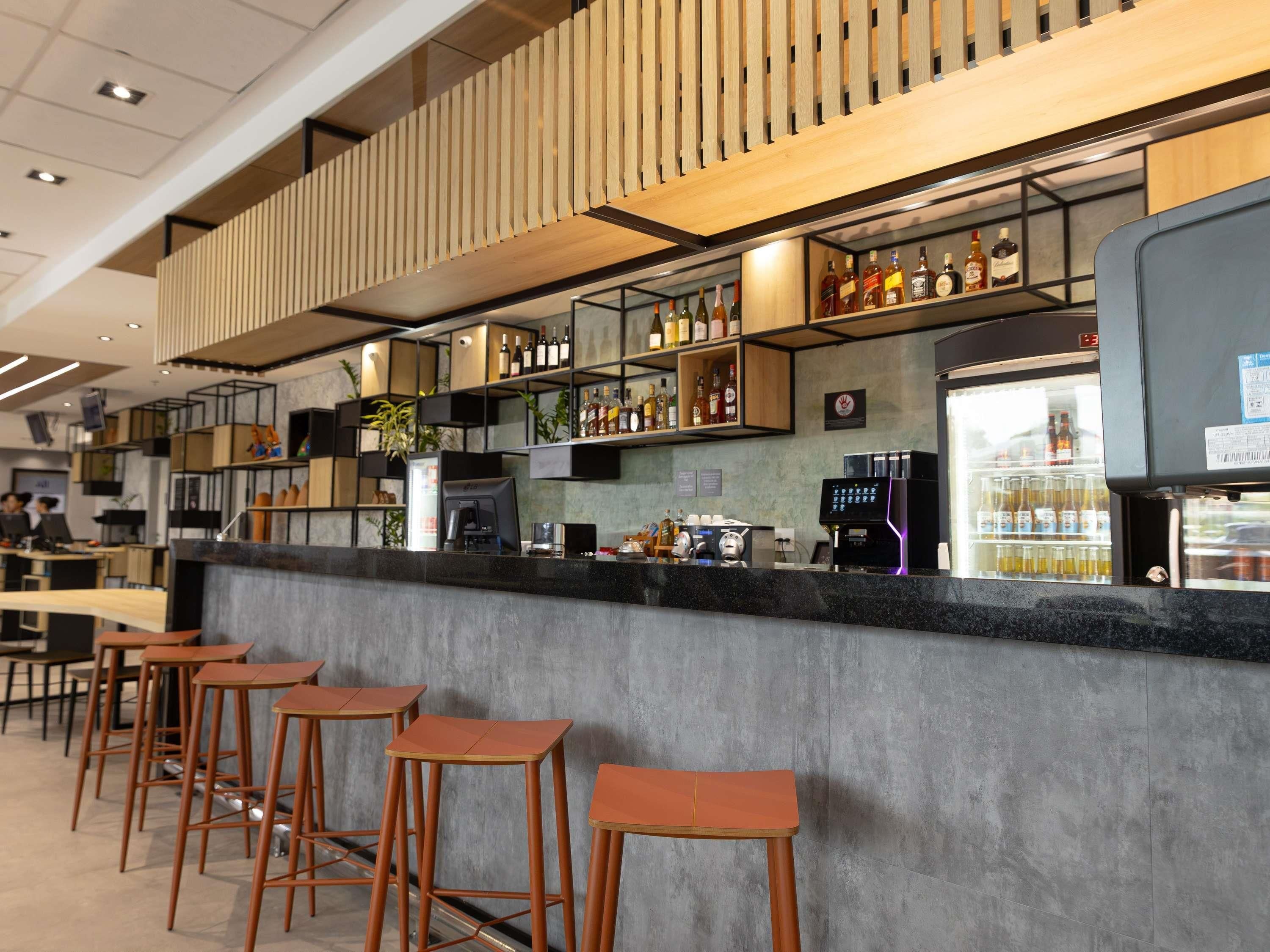 Uma área de bar com banquetas, prateleiras cheias de garrafas e uma máquina de café.