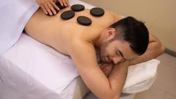 Uma pessoa recebendo uma massagem nas costas com várias pedras pretas colocadas sobre elas.