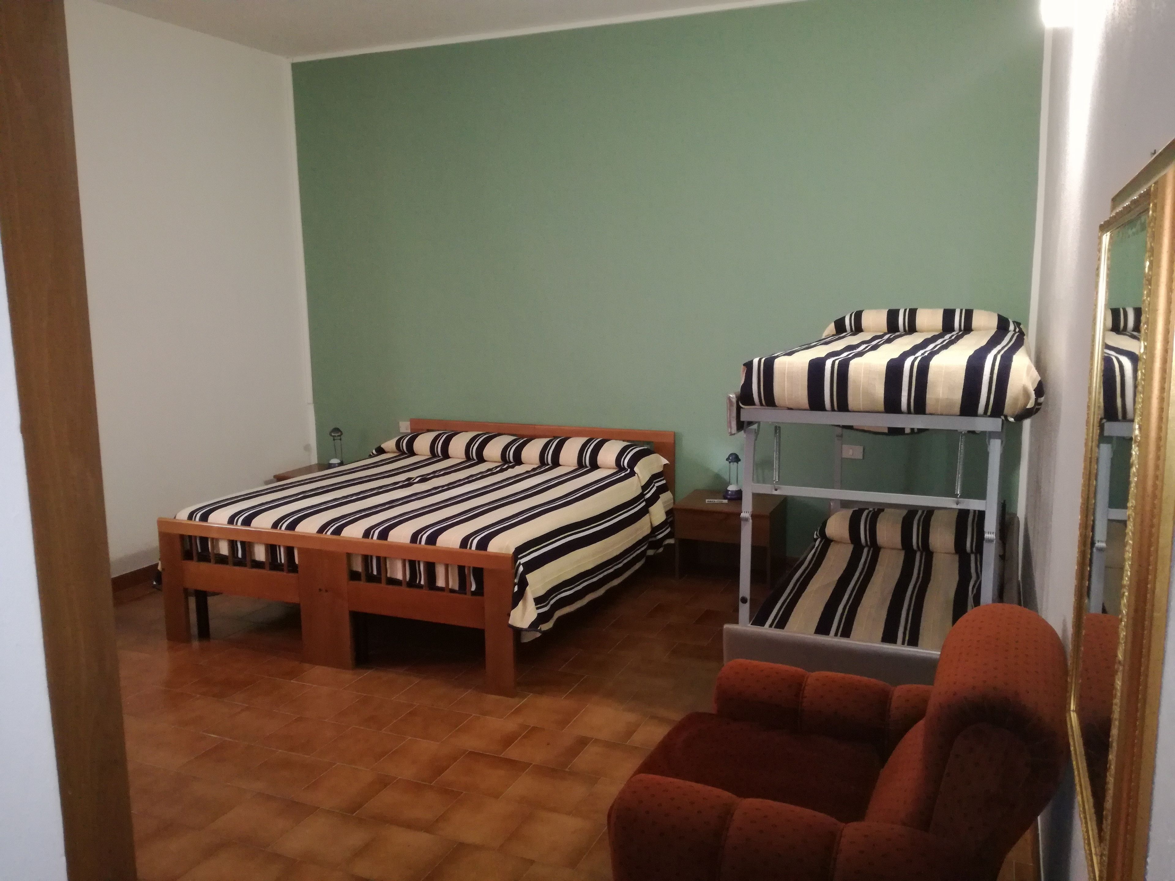 Quarto com cama de madeira, beliche e uma cadeira vermelha.
