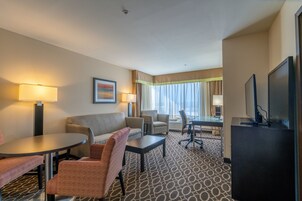 Quarto de hotel com sofá, poltronas, mesa pequena, escrivaninha com cadeira, televisão e carpete estampado.