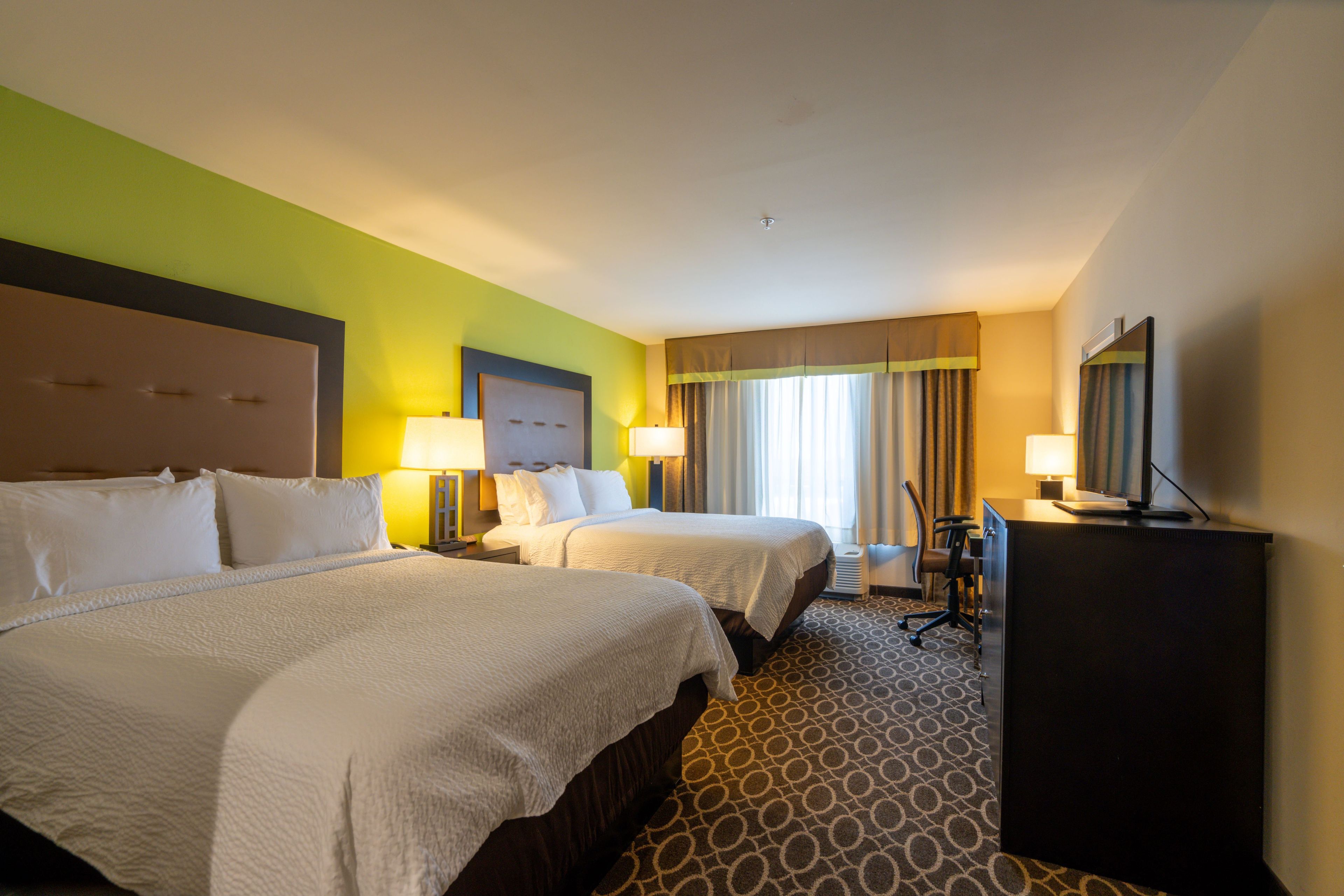 Quarto de hotel com duas camas, uma escrivaninha, televisão e janela com cortinas.