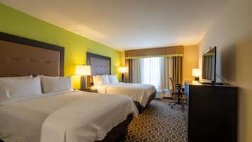 Quarto de hotel com duas camas, uma escrivaninha, televisão e janela com cortinas.