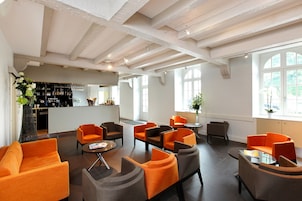 Um hall amplo com assentos modernos em tons de laranja e cinza, área de bar com prateleiras cheias de garrafas e grandes janelas que proporcionam iluminação natural.