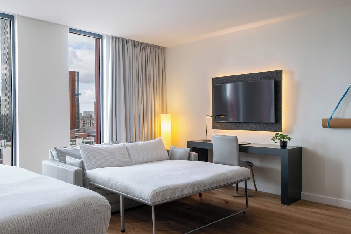 Quarto de hotel moderno com cama, escrivaninha, cadeira, televisão e vista para a cidade.