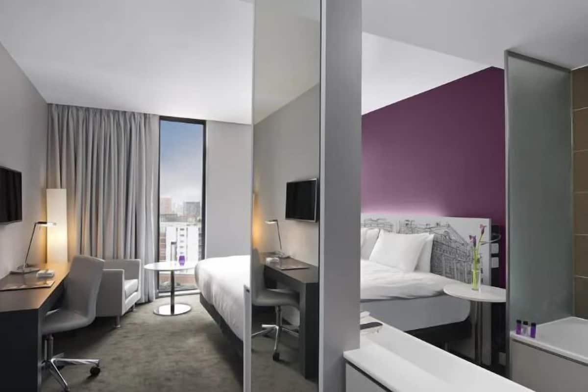 Quarto de hotel moderno com cama, escrivaninha, cadeira e uma pequena mesa.
