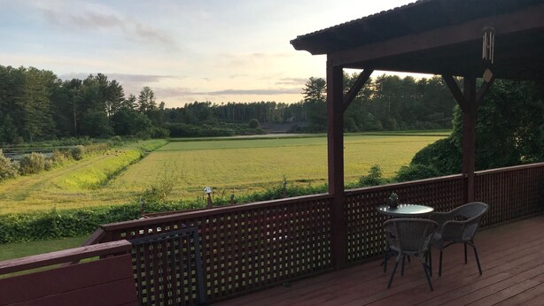 Um deck de madeira com mesa e cadeiras, com vista para um campo verde e árvores.