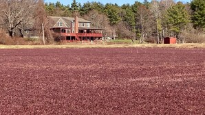 Uma casa grande com varanda vermelha, rodeada por árvores e um campo.