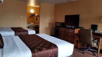 Quarto de hotel com duas camas, uma escrivaninha com computador, televisão e uma cadeira.