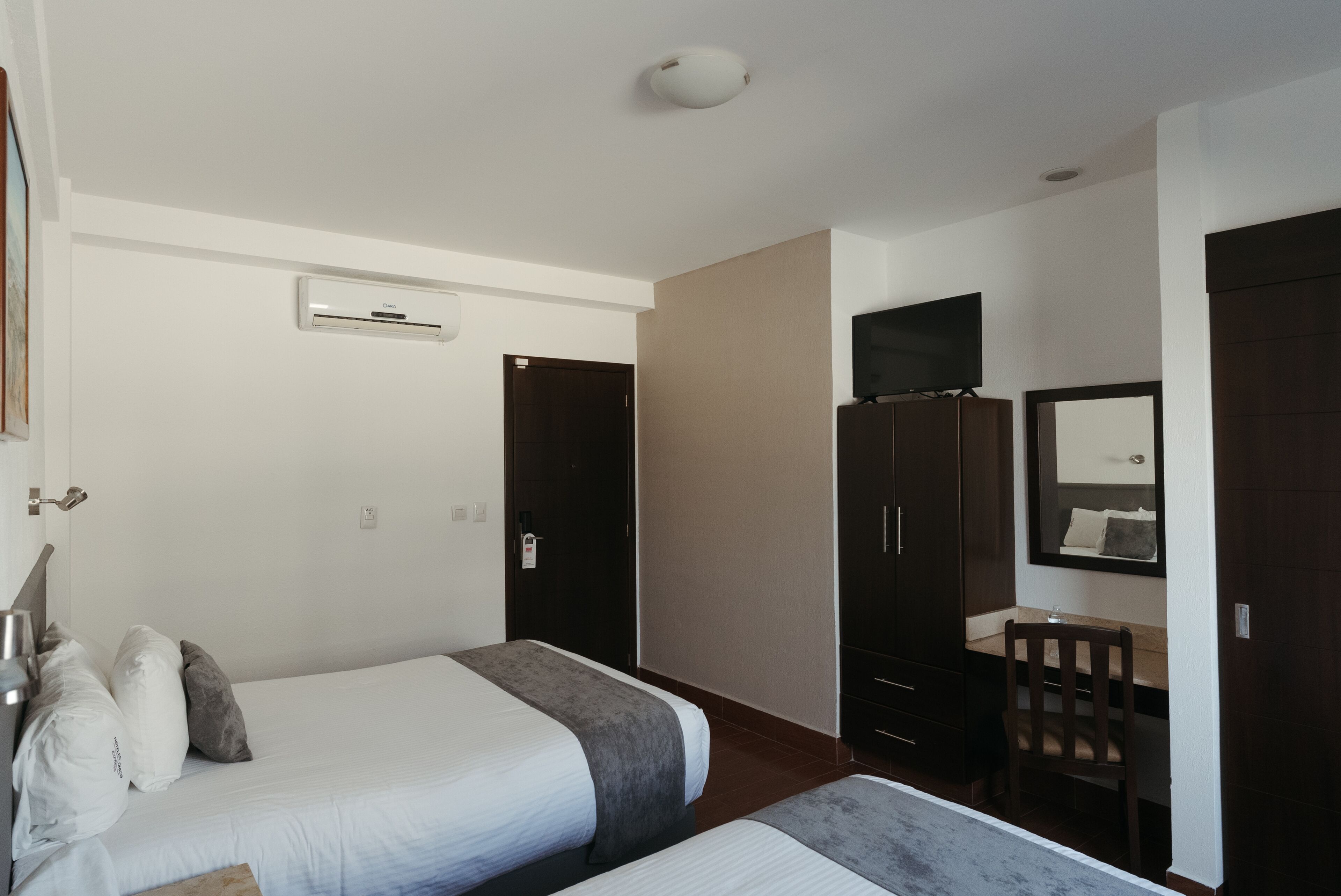 Quarto com cama, escrivaninha, cadeira, televisão e guarda-roupa.