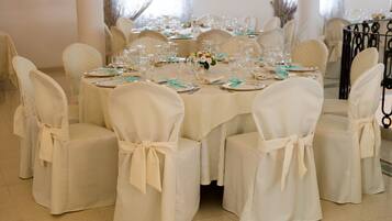 Disposição formal para refeições com mesas redondas, cadeiras brancas e ambiente elegante e impecável.