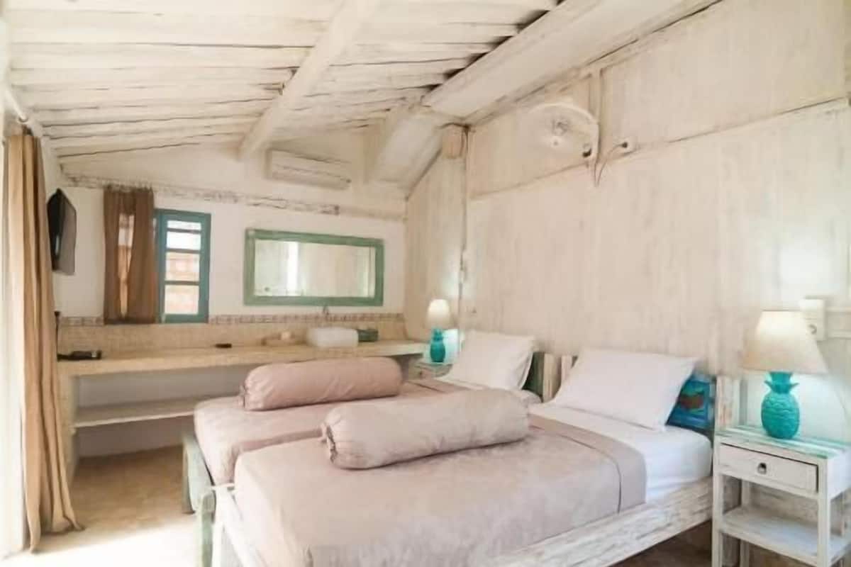 Quarto com teto de madeira, um espelho grande, duas camas, uma escrivaninha e uma mesa de cabeceira com abajur.