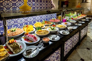 Buffet com diversos pratos, utensílios e painel decorativo de azulejos.