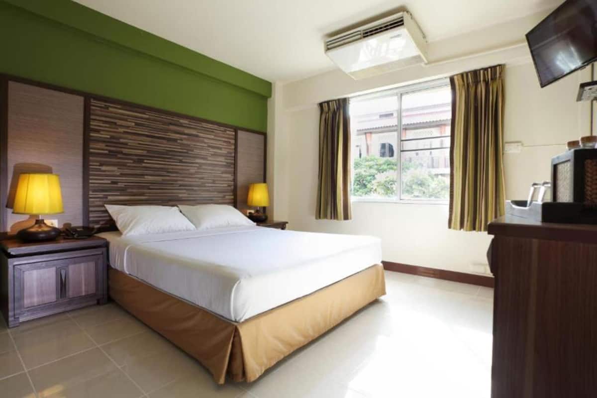 Quarto de hotel com uma cama grande, duas luminárias de cabeceira, uma TV e uma janela com cortinas.