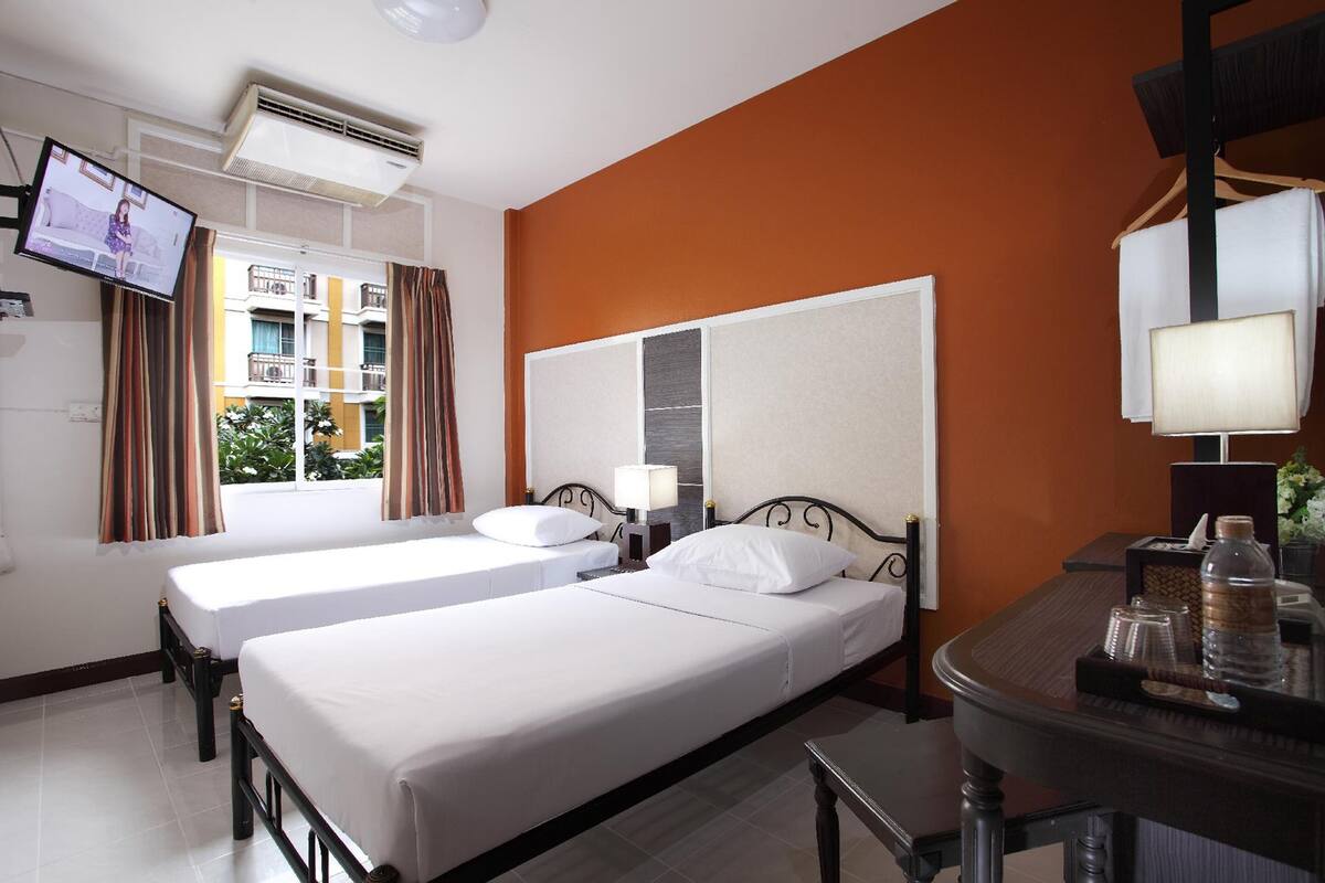 Quarto de hotel com duas camas, televisão, escrivaninha e janela com cortinas.