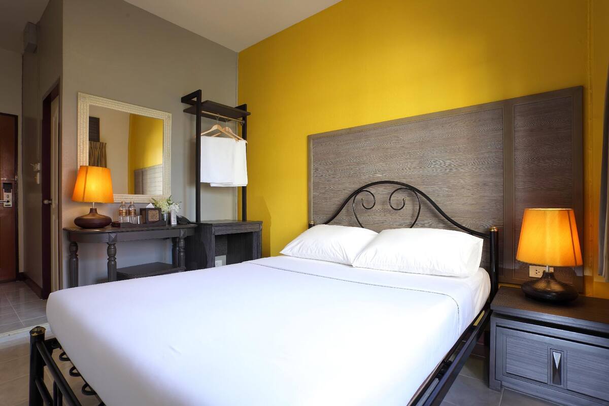 Quarto de hotel com uma cama, mesas de cabeceira, escrivaninha e espelho.