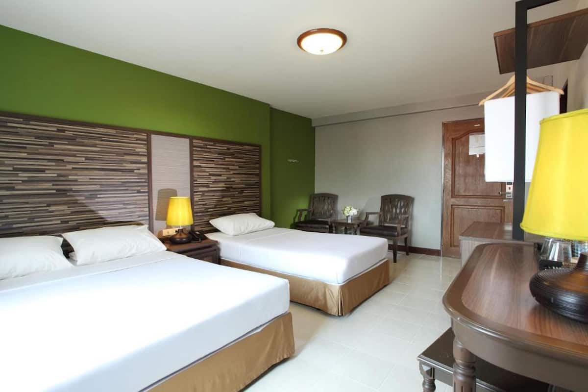 Quarto de hotel com duas camas, uma cabeceira de madeira, uma escrivaninha com abajur e uma cadeira.