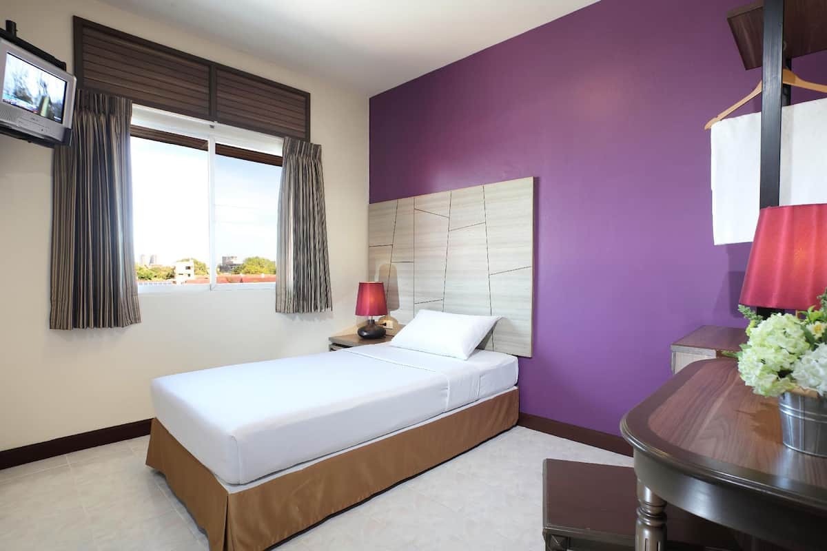 Quarto de hotel com cama, mesa de cabeceira com abajur, janela com cortinas e vista para o exterior.