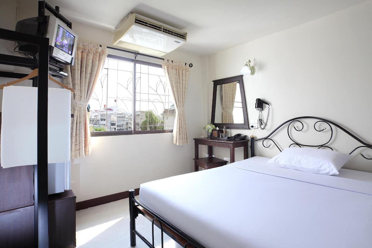 Quarto de hotel com cama, escrivaninha com computador, janela com cortinas e espelho fixado na parede.