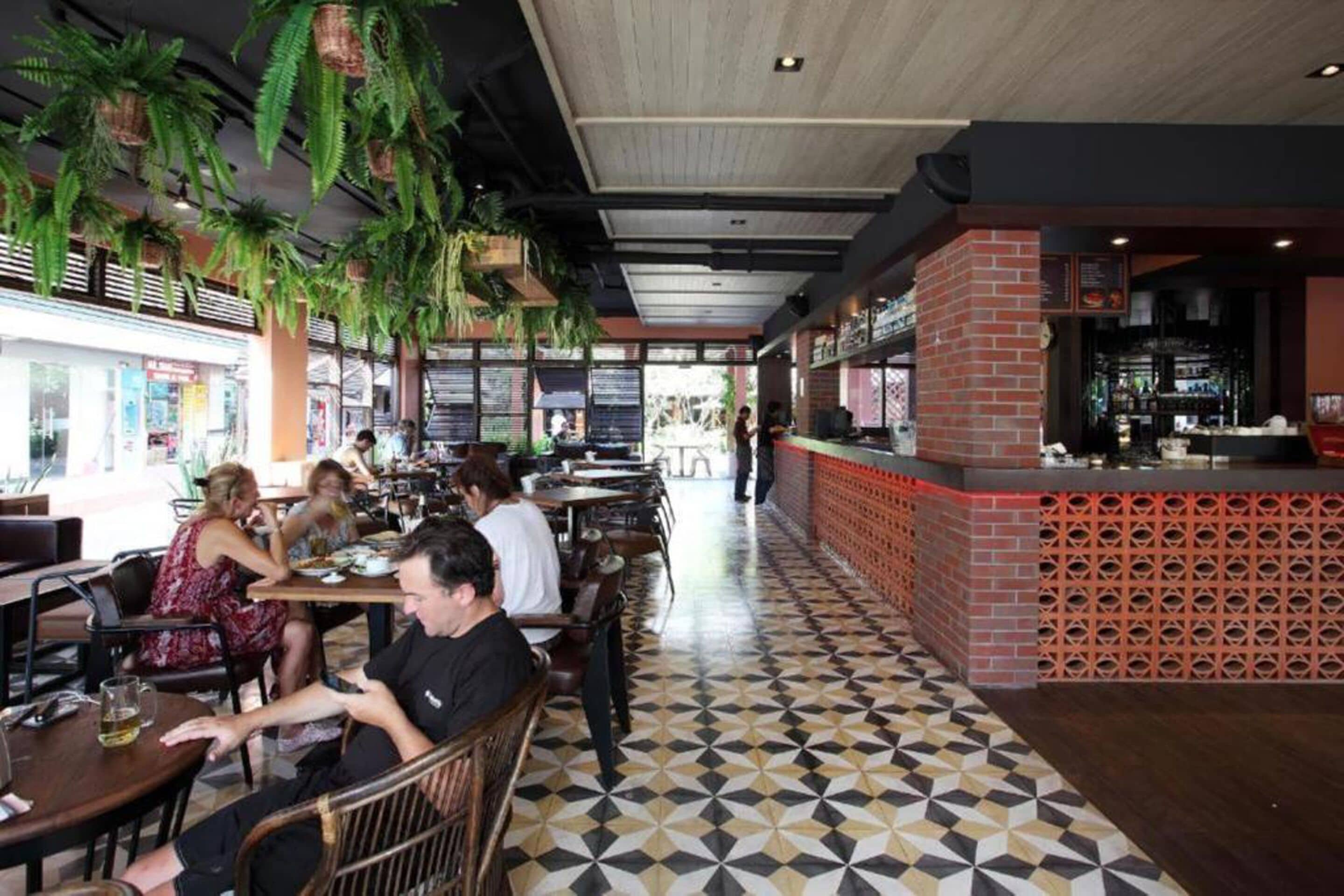 Restaurante com plantas internas, piso estampado e balcão de tijolos.