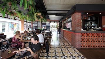 Restaurante com plantas internas, piso estampado e balcão de tijolos.