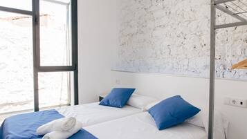Quarto de hotel com uma cama, duas almofadas, uma toalha enrolada, uma janela e uma parede com textura.