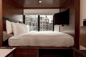 Quarto de hotel moderno com uma cama grande, televisão de tela plana e vista para edifícios da cidade.