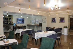 Um restaurante com várias mesas e cadeiras, um espaço de bar e obras de arte nas paredes.