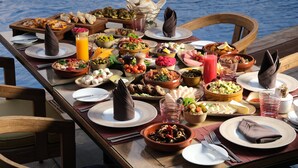 Mesa posta com diversos pratos e bebidas, com vista para um corpo de água.