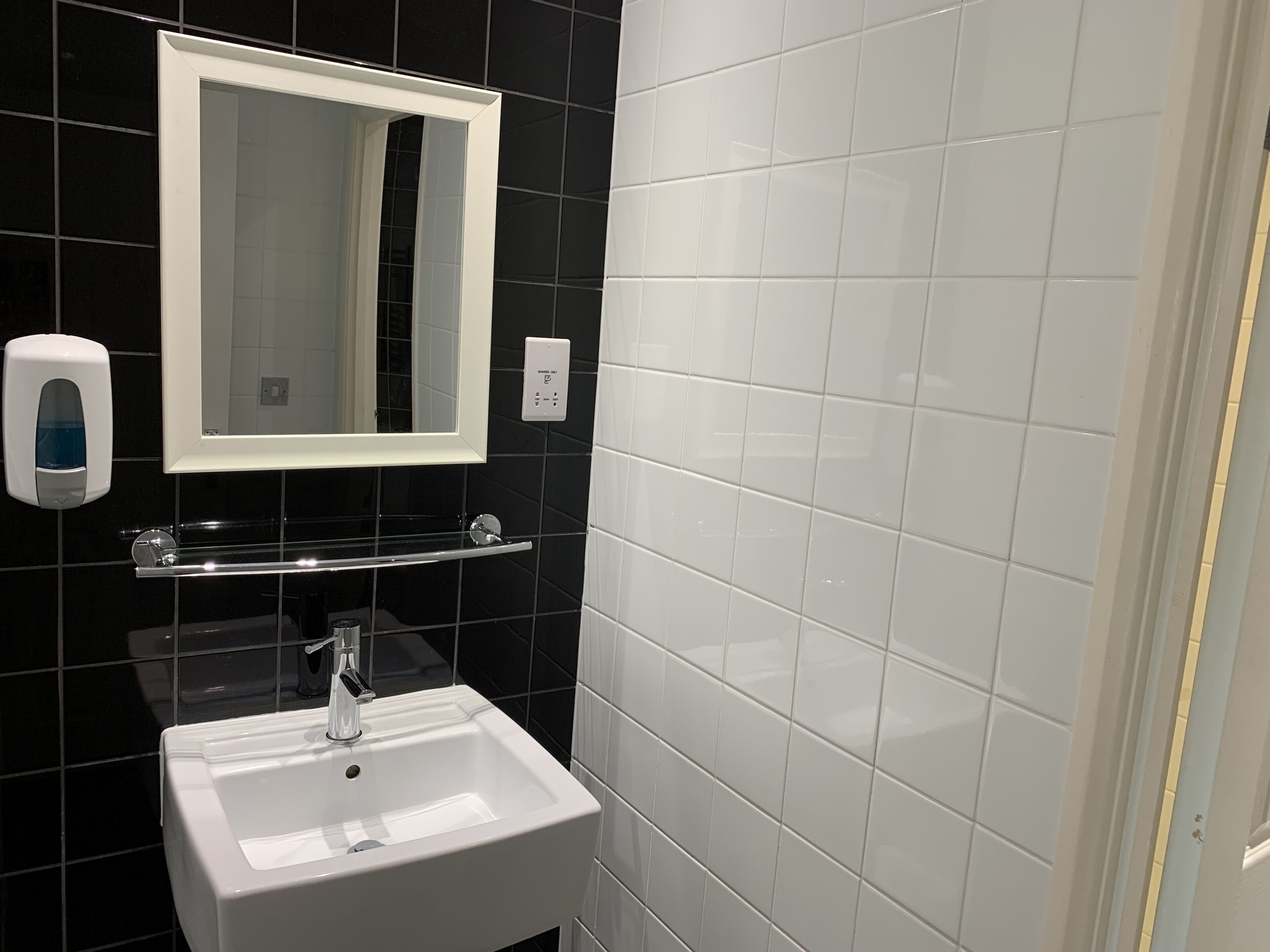 Casa de banho com lavatório branco, espelho e dispensador de sabonete.