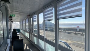 Um corredor com assentos, janelas amplas e vista para um aeroporto.