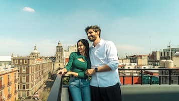 Um casal em uma varanda com vista para um horizonte urbano repleto de edifícios históricos e céu claro.