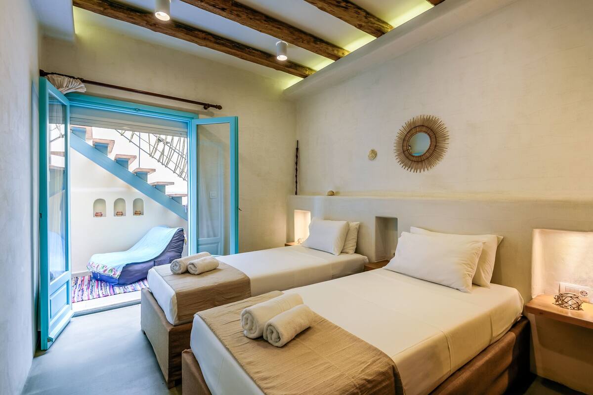 Quarto de hotel com duas camas, escada que dá para área externa e um painel decorativo na parede.