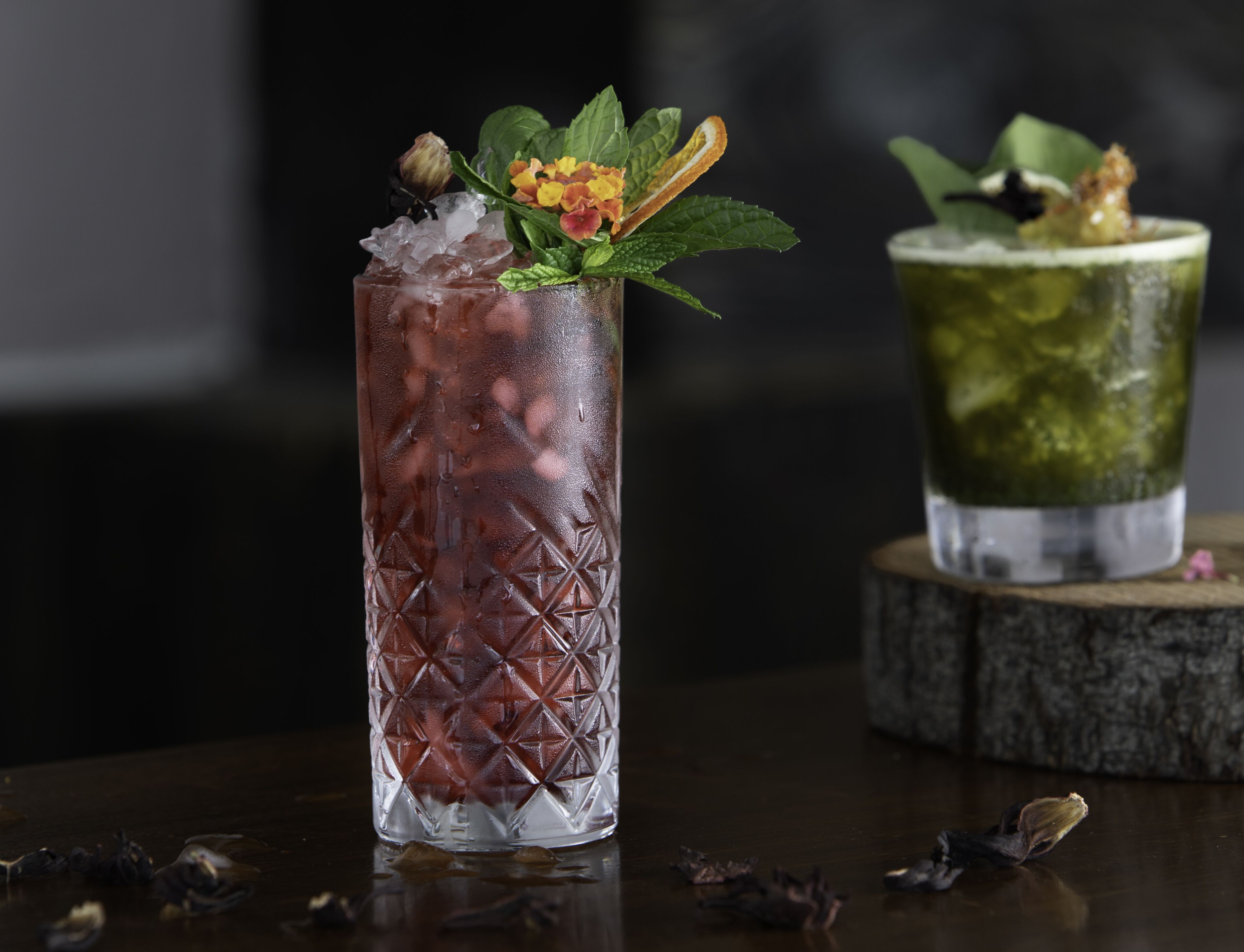 Duas taças altas de bebidas geladas com guarnições, apoiadas em uma superfície de madeira.