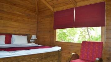 Quarto de cabana de madeira com cama, uma cadeira e janela com vista para vegetação.