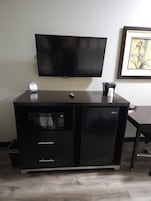 Uma unidade de entretenimento preta com uma TV de tela plana montada acima, um controle remoto pequeno e um quadro na parede.