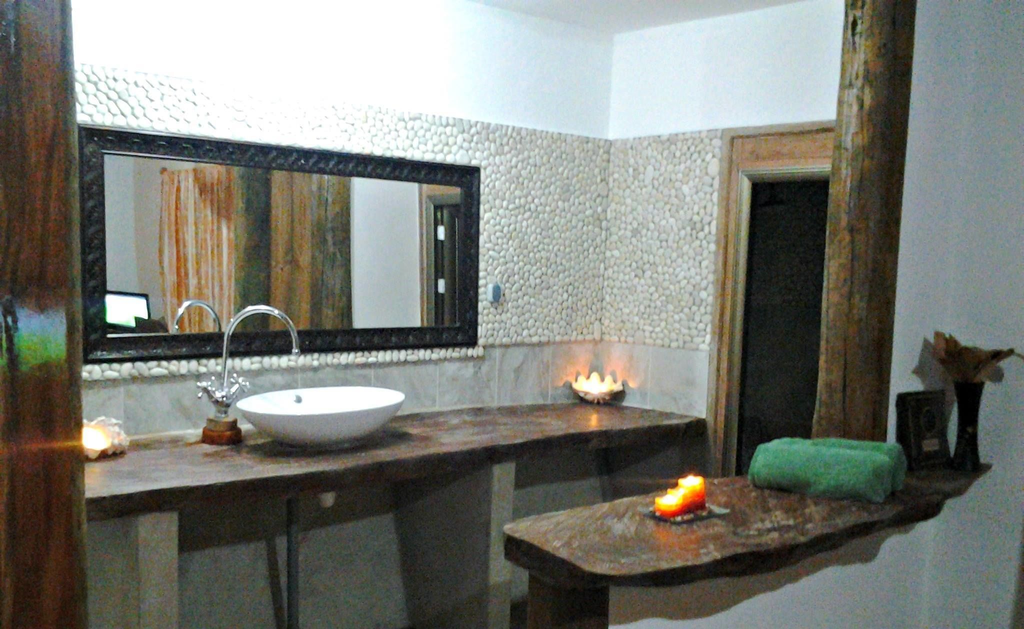 Casa de banho com lavatório branco, espelho e prateleira com uma vela e uma toalha.