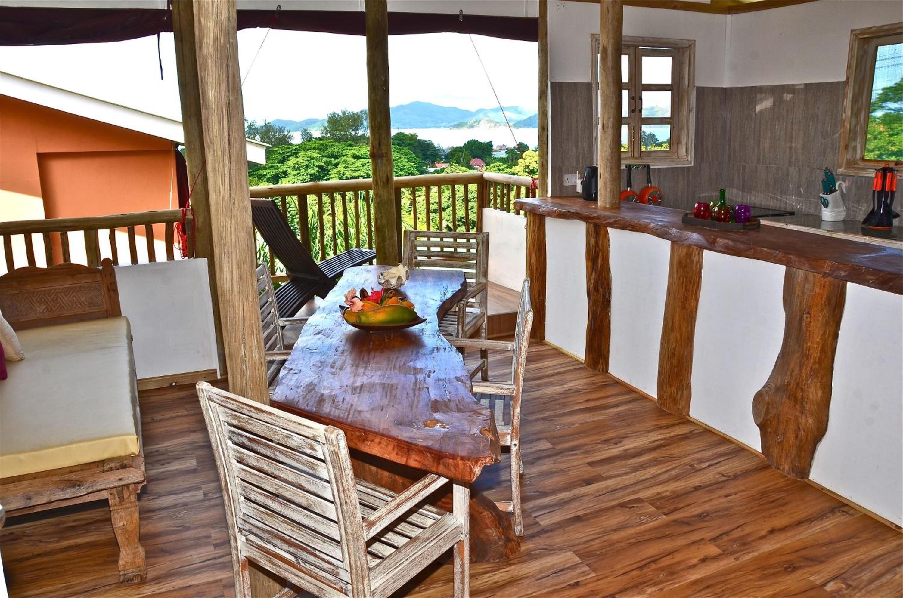 Uma mesa de jantar de madeira com cadeiras, uma tigela pequena e vista para montanhas e vegetação.