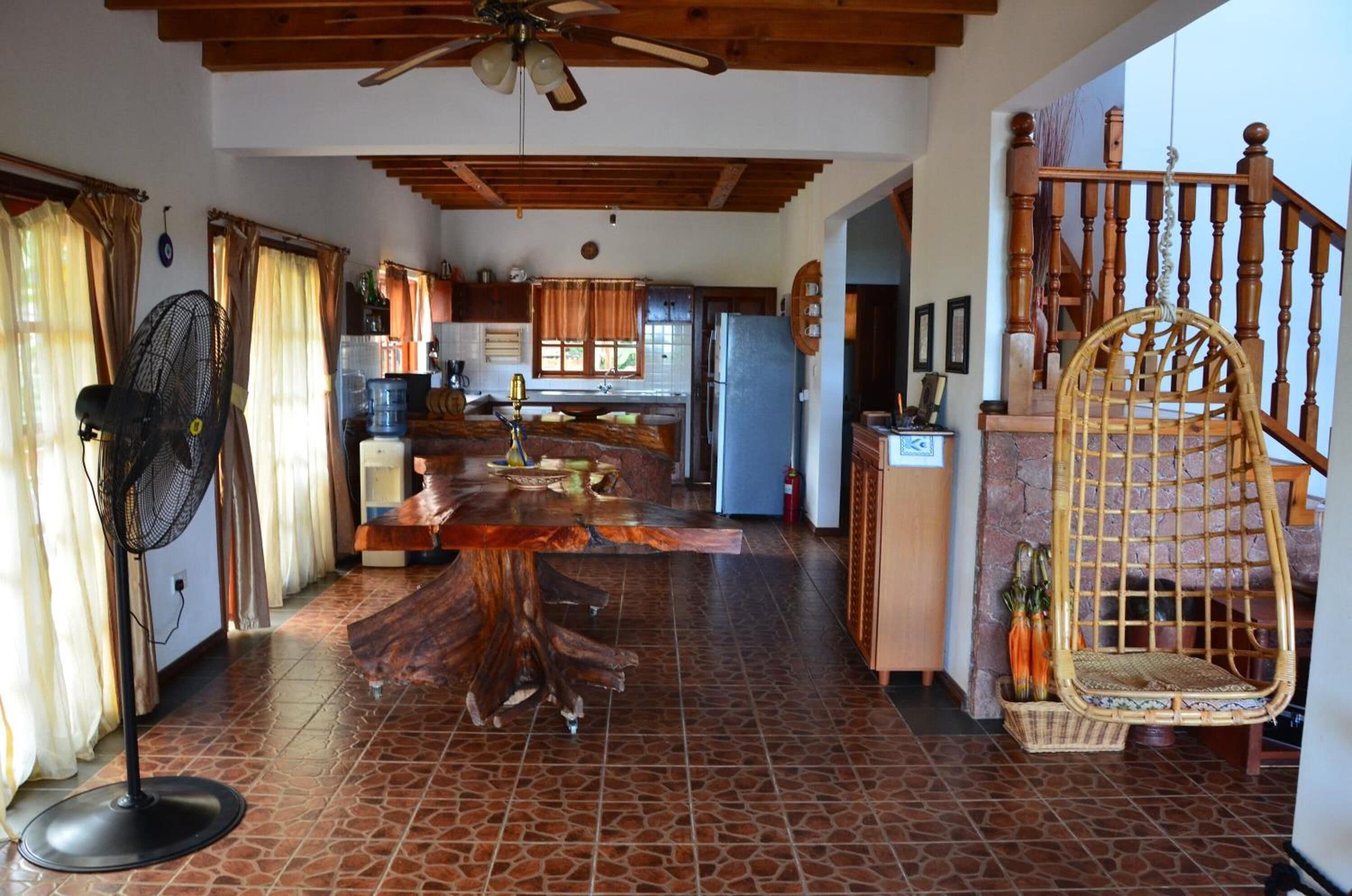 Uma cozinha ampla com uma ilha grande, vigas de madeira no teto e uma cadeira de vime perto da escada.