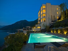 Um hotel com piscina, espreguiçadeiras e vista para o lago e as montanhas.